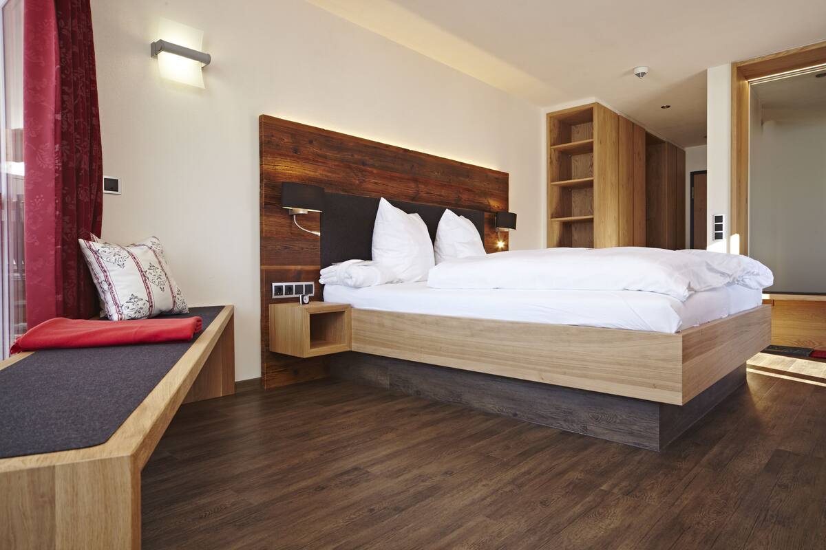 Quarto moderno com cabeceira de madeira, mesa de cabeceira com abajur e um banco embutido.