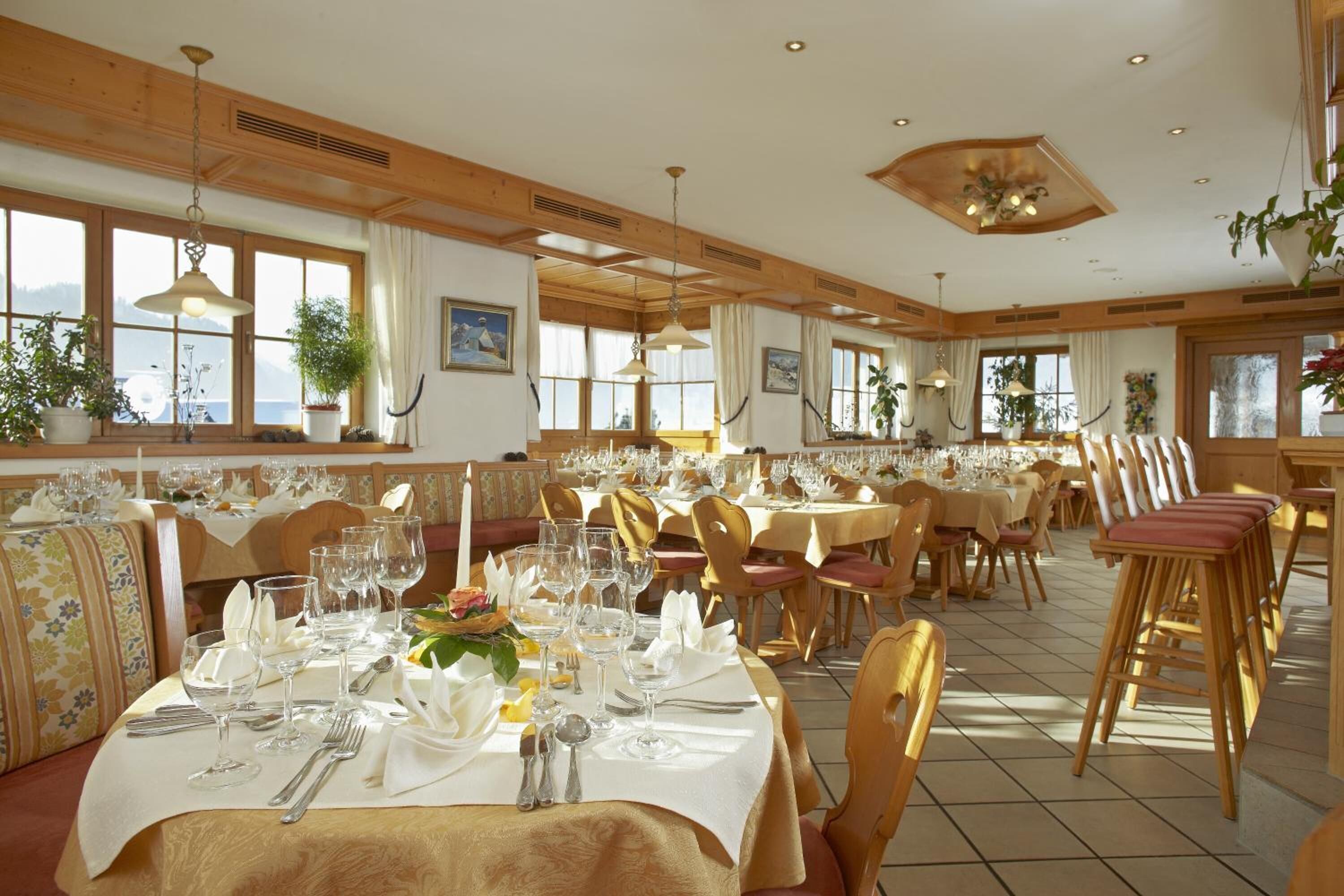 Restaurante com várias mesas e cadeiras, grandes janelas com vista e decoração em madeira.