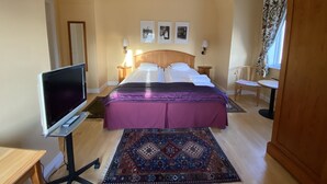 Quarto de hotel com cama, televisão, escrivaninha e cadeira.