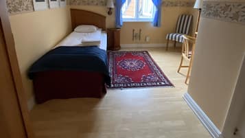 Quarto com cama, mesa de cabeceira, cadeira, janela com cortinas e luminária na parede.