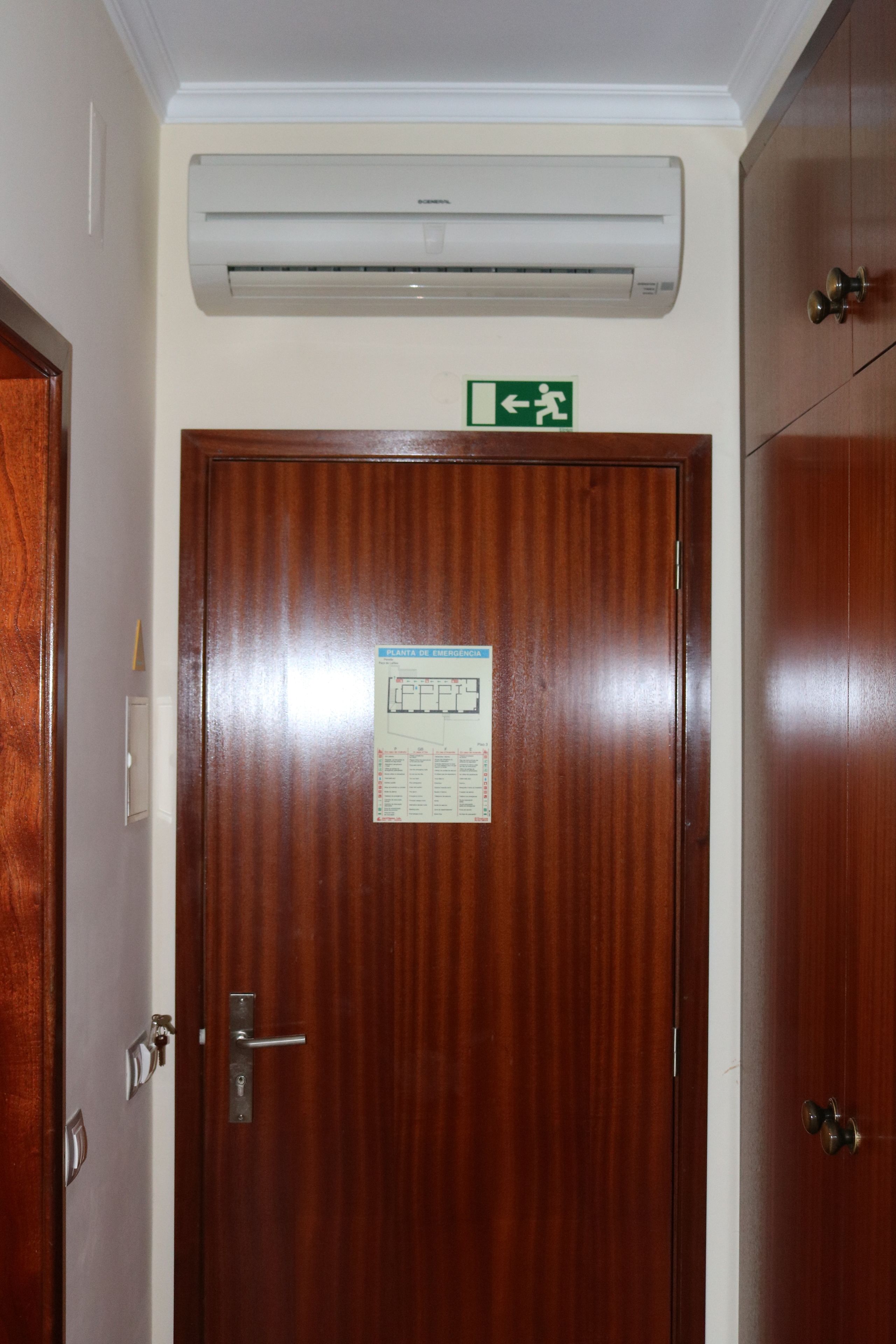 Uma porta de madeira com placa de saída de emergência verde e um aviso afixado.