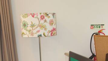 Um quarto com uma cadeira estofada verde, um banquinho pequeno, uma luminária floral e um extintor de CO2 na parede.