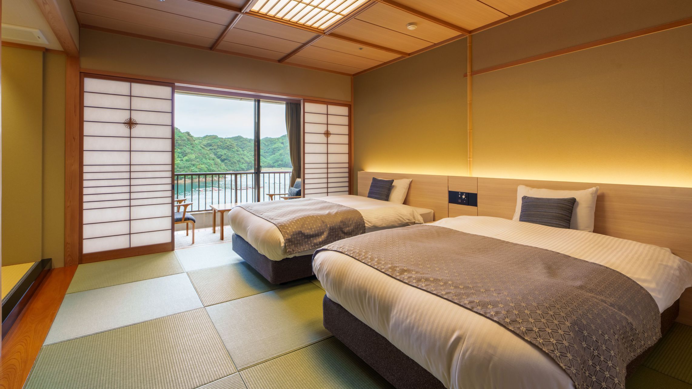 Quarto de hotel com duas camas, piso de tatame, varanda com vista e porta tradicional japonesa deslizante.