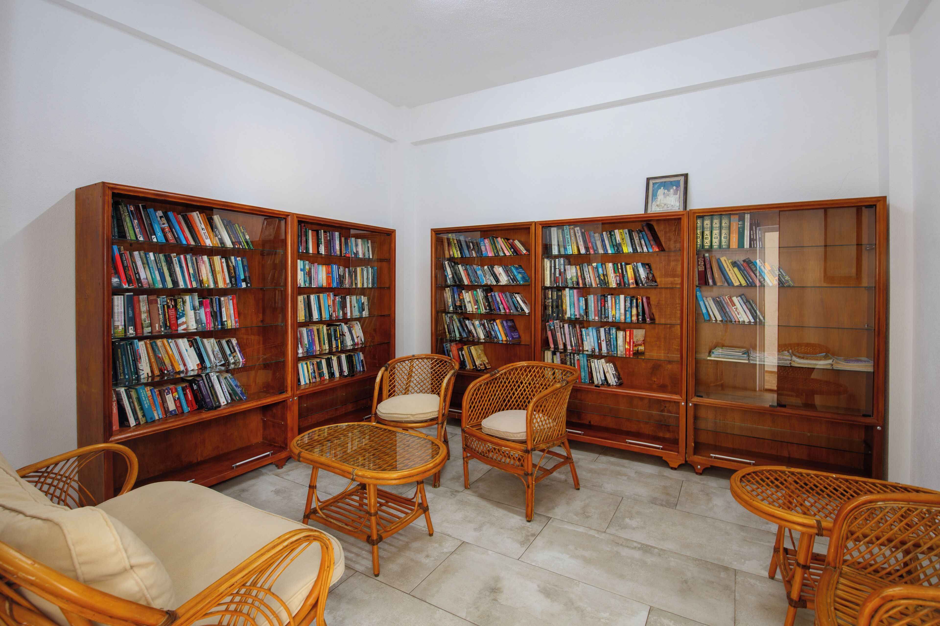 Um quarto com um sofá, três cadeiras de vime e uma estante repleta de livros.