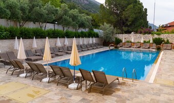Área de piscina com espreguiçadeiras e guarda-sóis, rodeada por vegetação e uma parede de pedra.