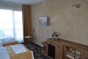 Quarto de hotel com duas camas, uma escrivaninha de madeira, uma cadeira e um quadro na parede.