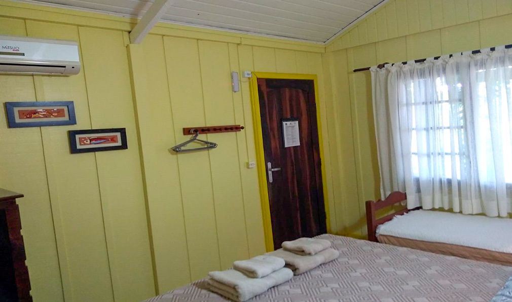 Quarto com duas camas, ar-condicionado fixado na parede, cabide e porta com uma placa.