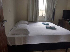 Quarto individual com janela, cortinas, televisão e porta.
