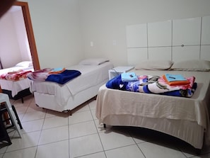 Quarto de hotel com duas camas de solteiro, uma mesinha e uma cadeira.