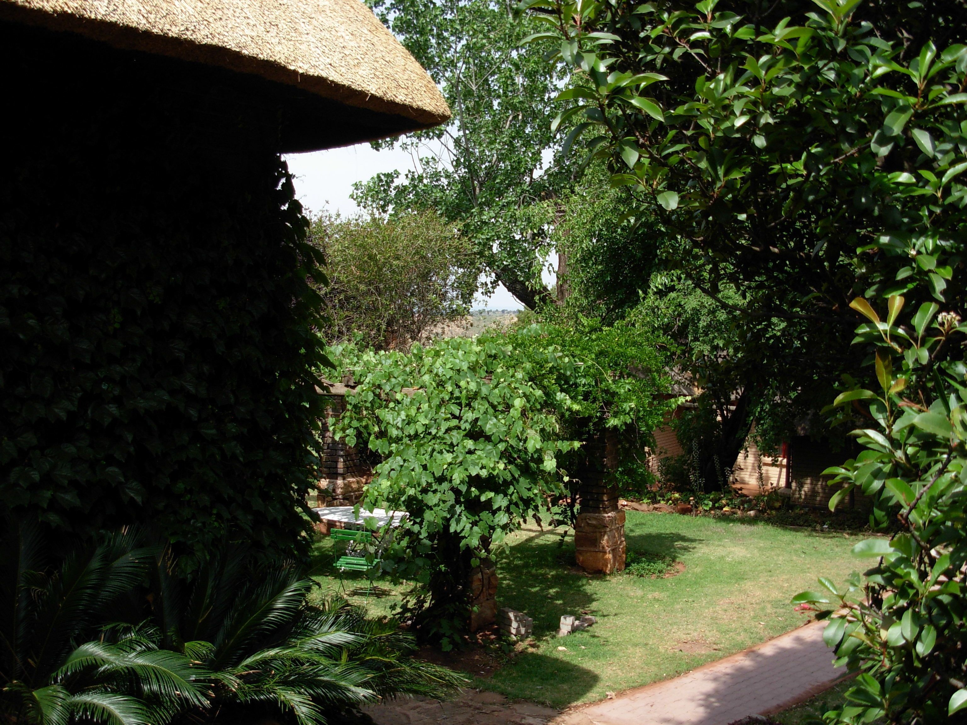 Um jardim com uma estrutura de telhado de palha, um pilar de pedra e um caminho pavimentado.