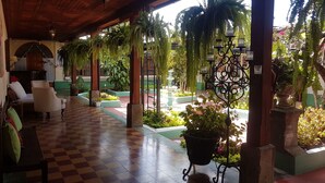 Um espaço coberto ao ar livre com piso xadrez, plantas em vasos e uma área de estar com cadeiras.