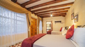 Quarto com cama grande, vigas de madeira, banheiro e piso xadrez.