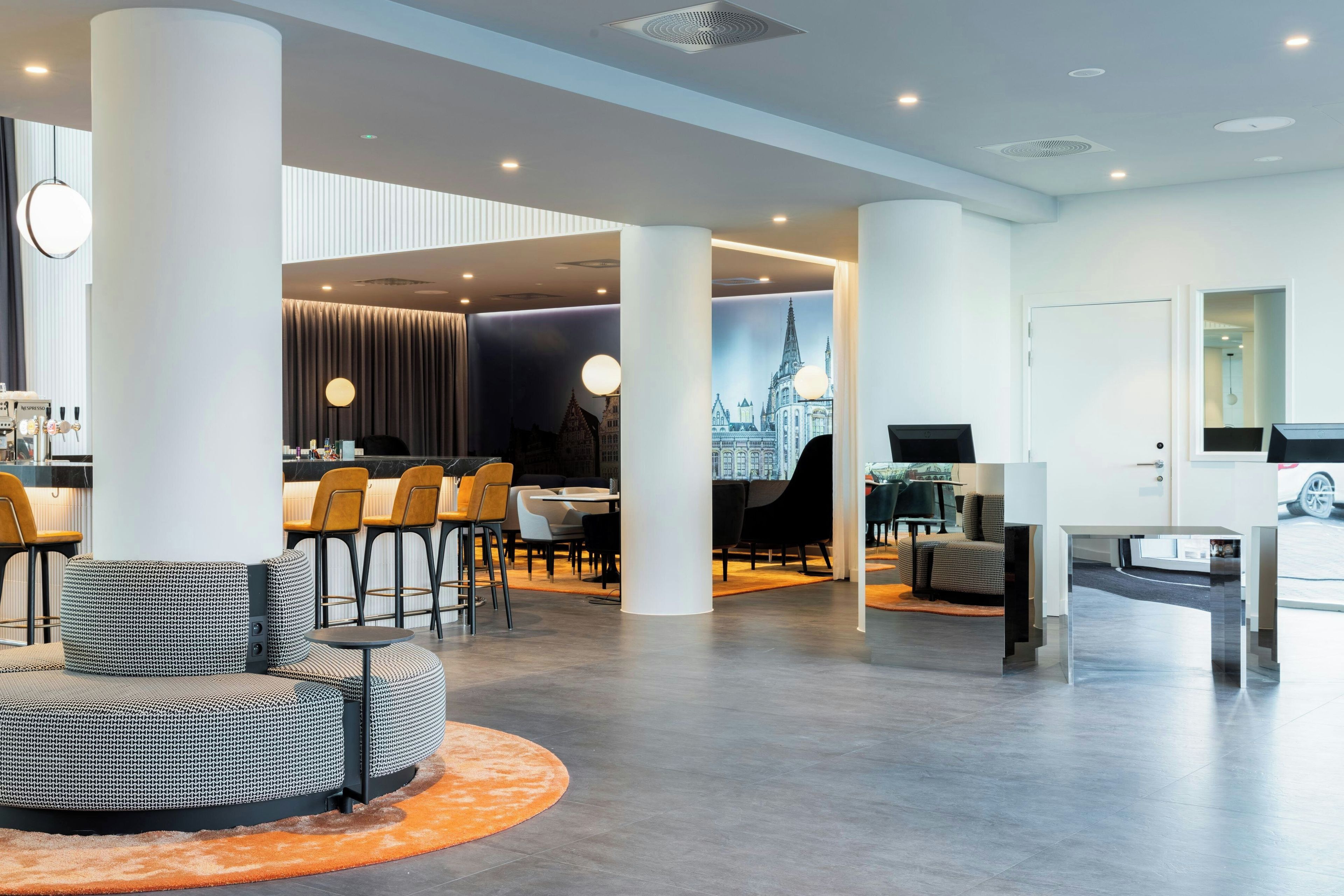 Um hall de hotel moderno com pé-direito alto, área de bar, espaços de estar e uma grande janela com vista para a paisagem urbana.