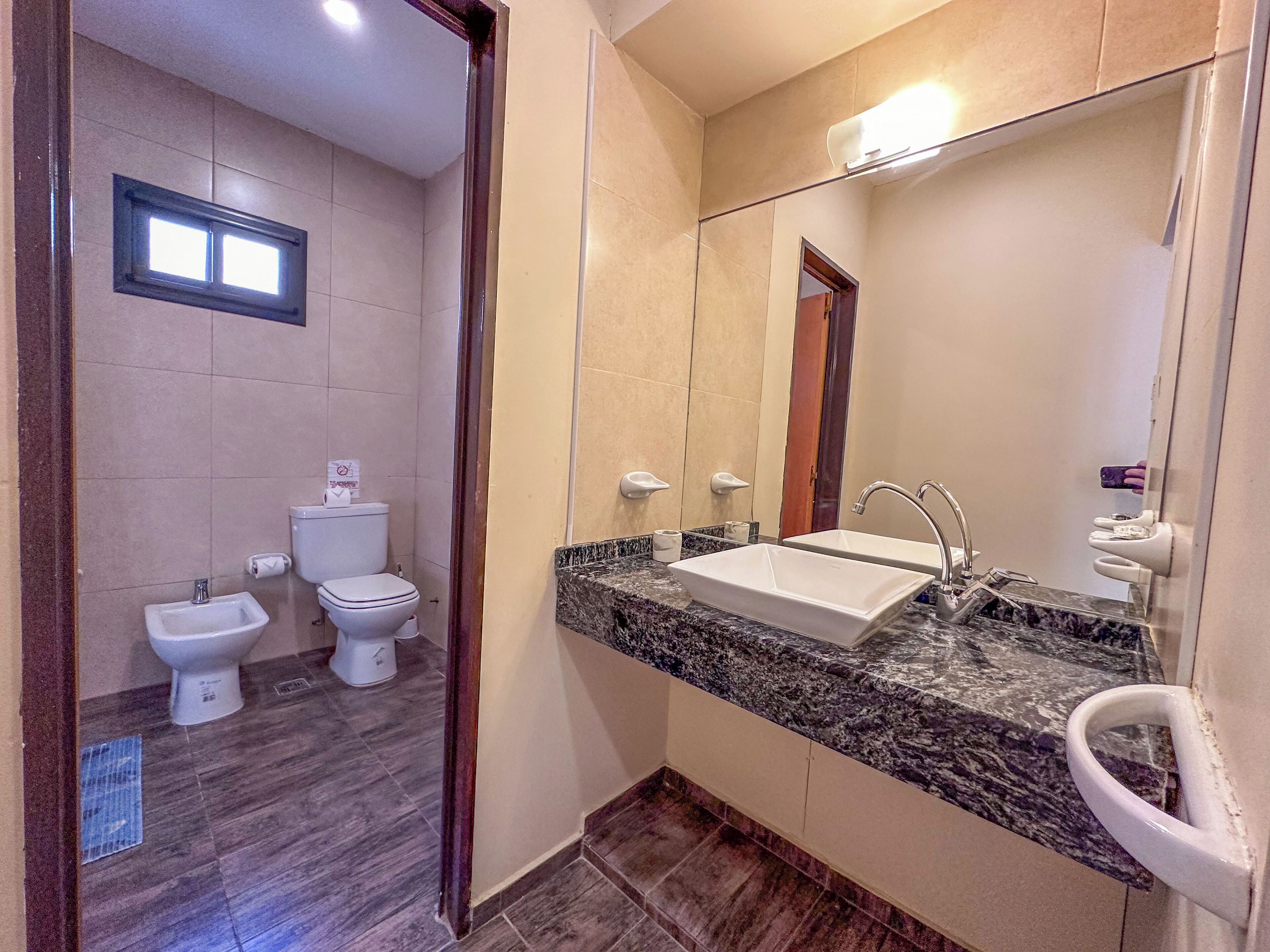 Um banheiro com bancada de mármore, pia, bidê e vaso sanitário.