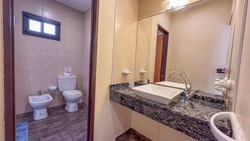 Um banheiro com bancada de mármore, pia, bidê e vaso sanitário.