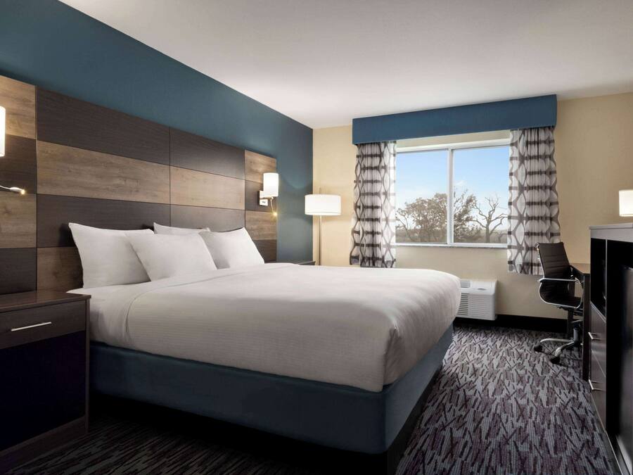 Quarto de hotel com uma cama grande, uma escrivaninha, uma cadeira e uma televisão.