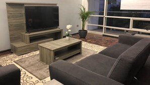 Uma sala de estar moderna com uma televisão de tela plana, um sofá, uma mesa de centro e um vaso com planta.
