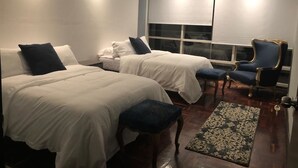 Quarto de hotel com duas camas, uma poltrona azul e uma janela grande.