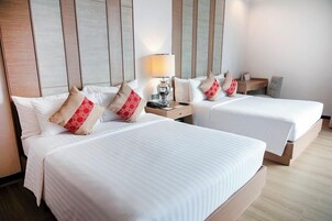 Quarto de hotel com duas camas de solteiro, cada uma com roupa de cama branca e almofadas de bolinhas vermelhas. Há uma mesa de cabeceira com uma luminária, um pequeno relógio e um telefone. O quarto tem uma cabeceira de madeira e piso em tom claro.