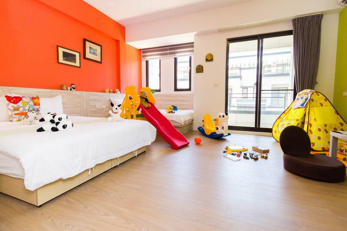 Quarto de hotel com cama, um escorrega vermelho e uma tenda amarela para brincar.