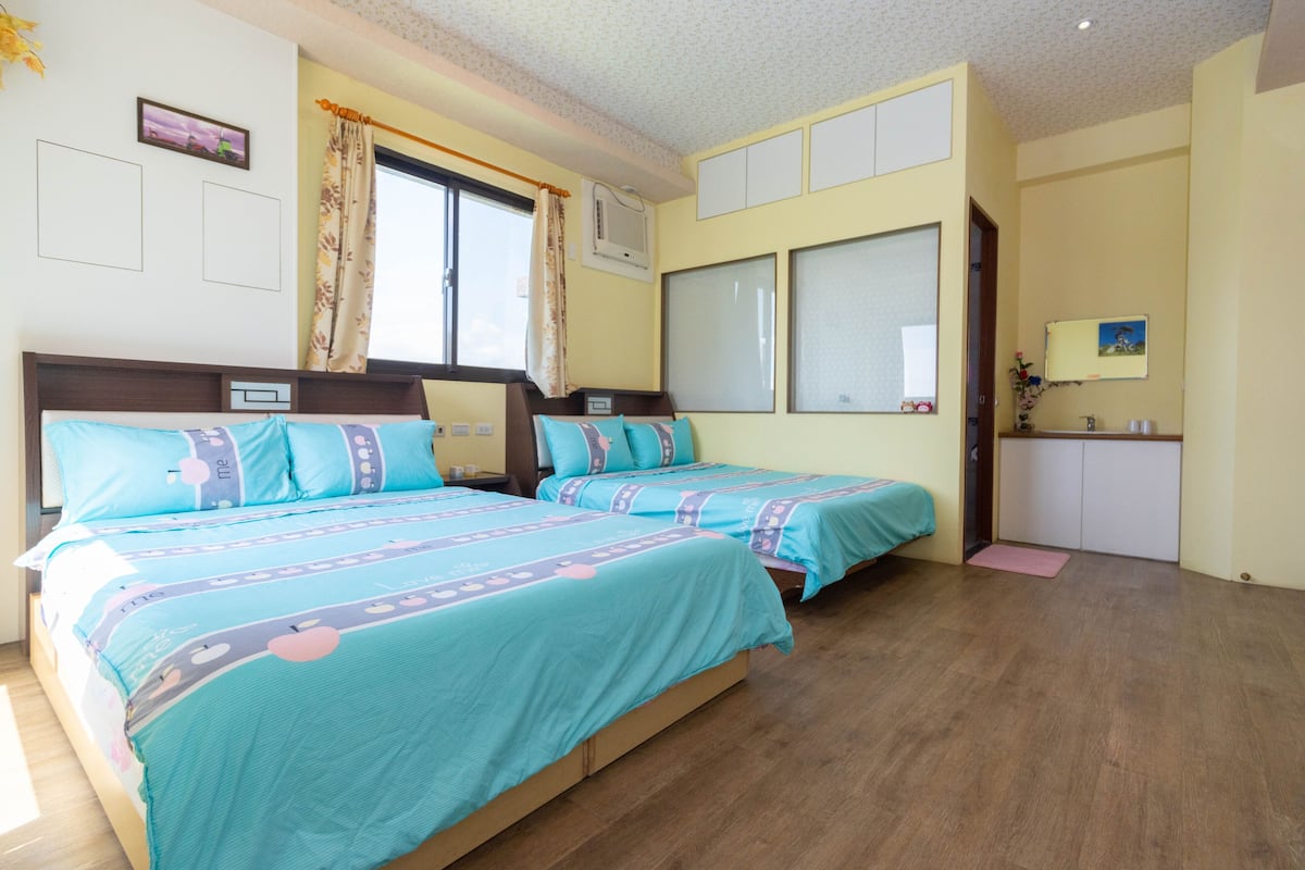 Quarto de hotel com duas camas, uma janela com cortinas, uma secretária pequena e um espelho.