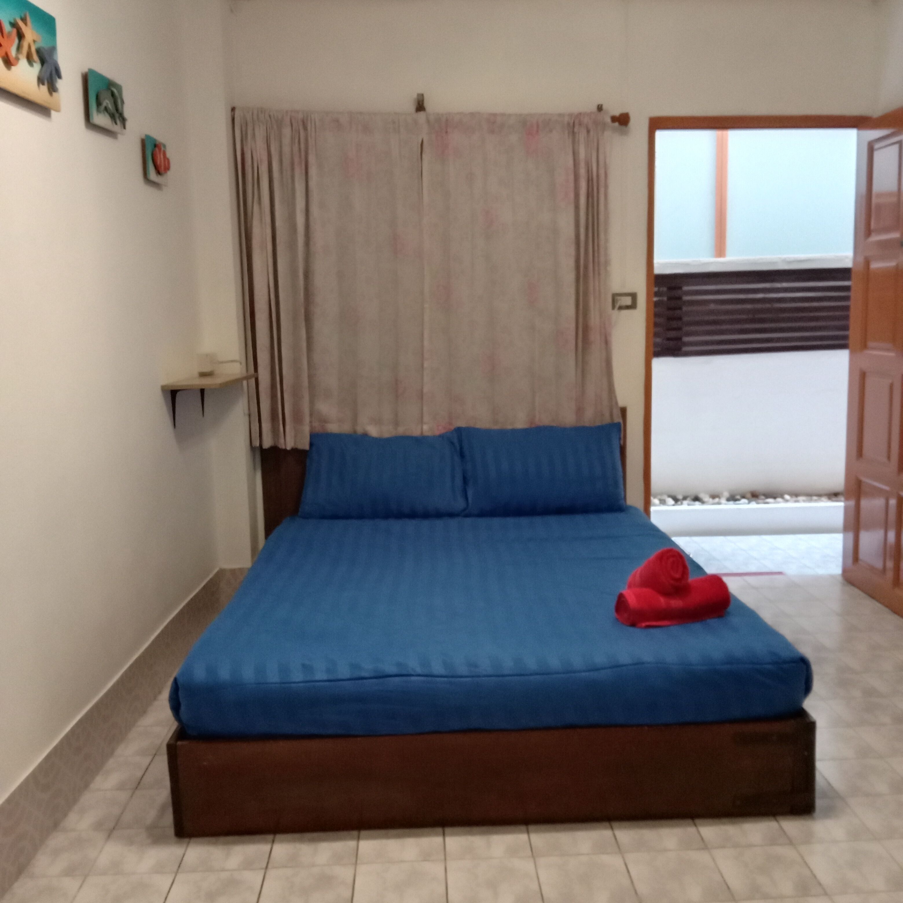 Quarto com cama, cabeceira de madeira, prateleira pequena e porta que dá para uma varanda.