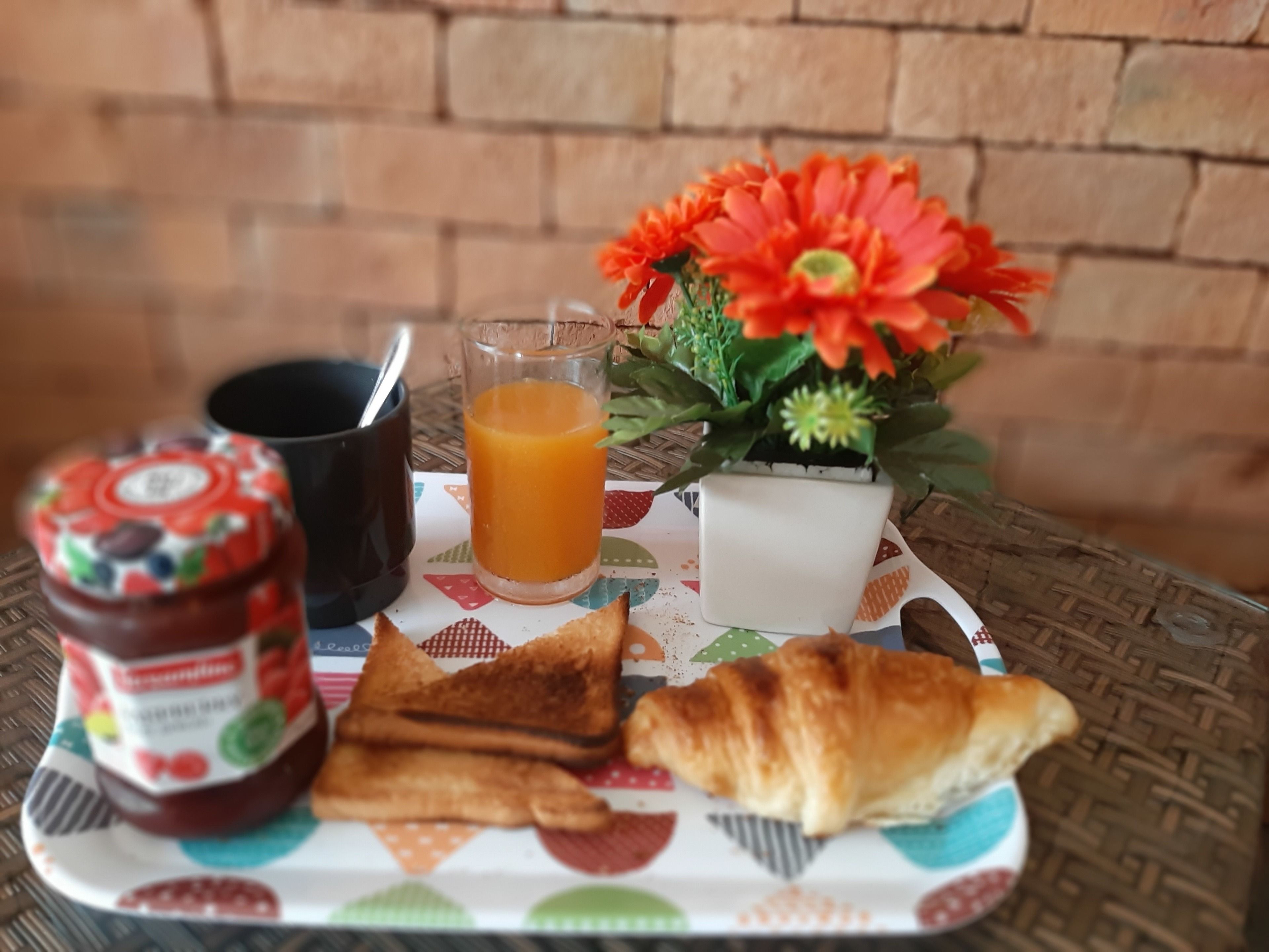 Uma bandeja de café da manhã com torradas, um croissant, um copo de suco de laranja, uma caneca e um pote de geleia.