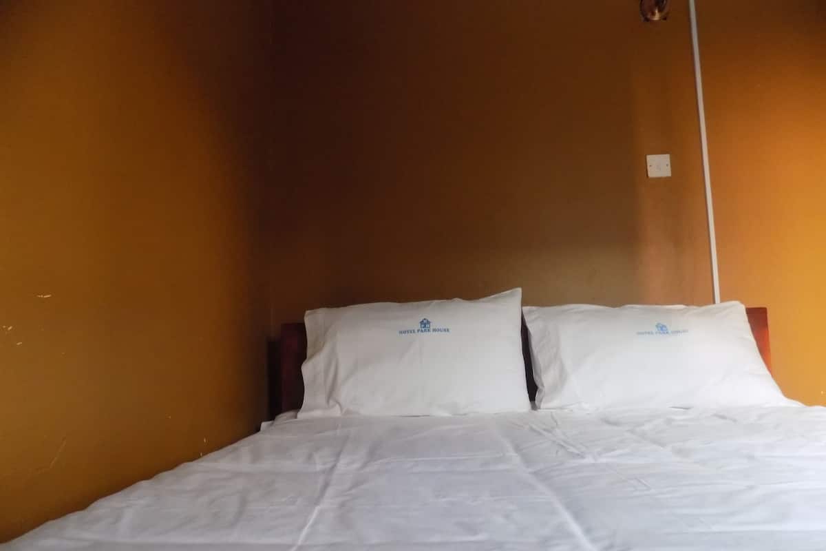 Uma cama de solteiro com roupa de cama e almofadas brancas, uma cabeceira de madeira e uma parede com tomada.