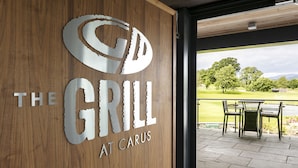Uma placa de madeira com o texto 'The Grill at Carus' e um logotipo.