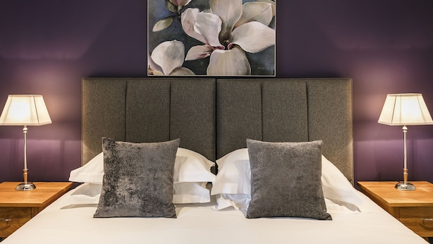 Quarto de hotel com uma cama grande, duas mesas de cabeceira e um quadro de flores na parede.