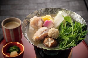 Uma tigela de sopa com diversos ingredientes, uma chávena de chá e um pequeno prato de vegetais.