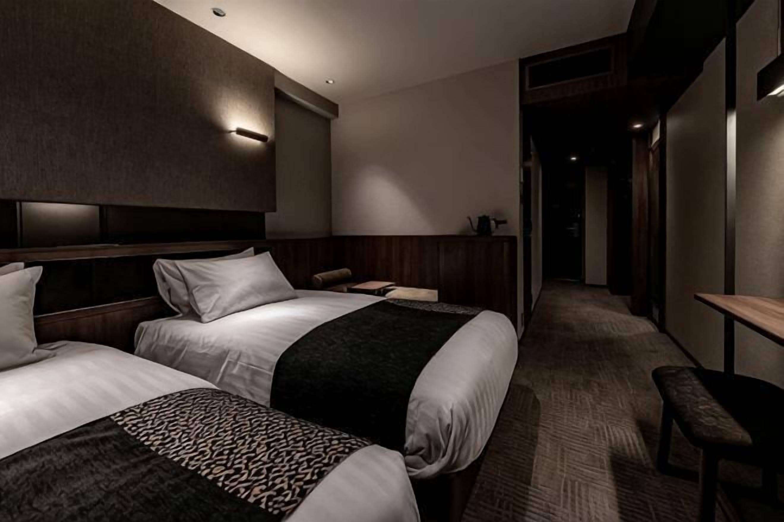 Quarto de hotel com duas camas, um banco, uma escrivaninha e um closet espaçoso.