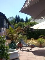 Uma área de pátio externa com uma espreguiçadeira, um guarda-sol grande e plantas em vasos.