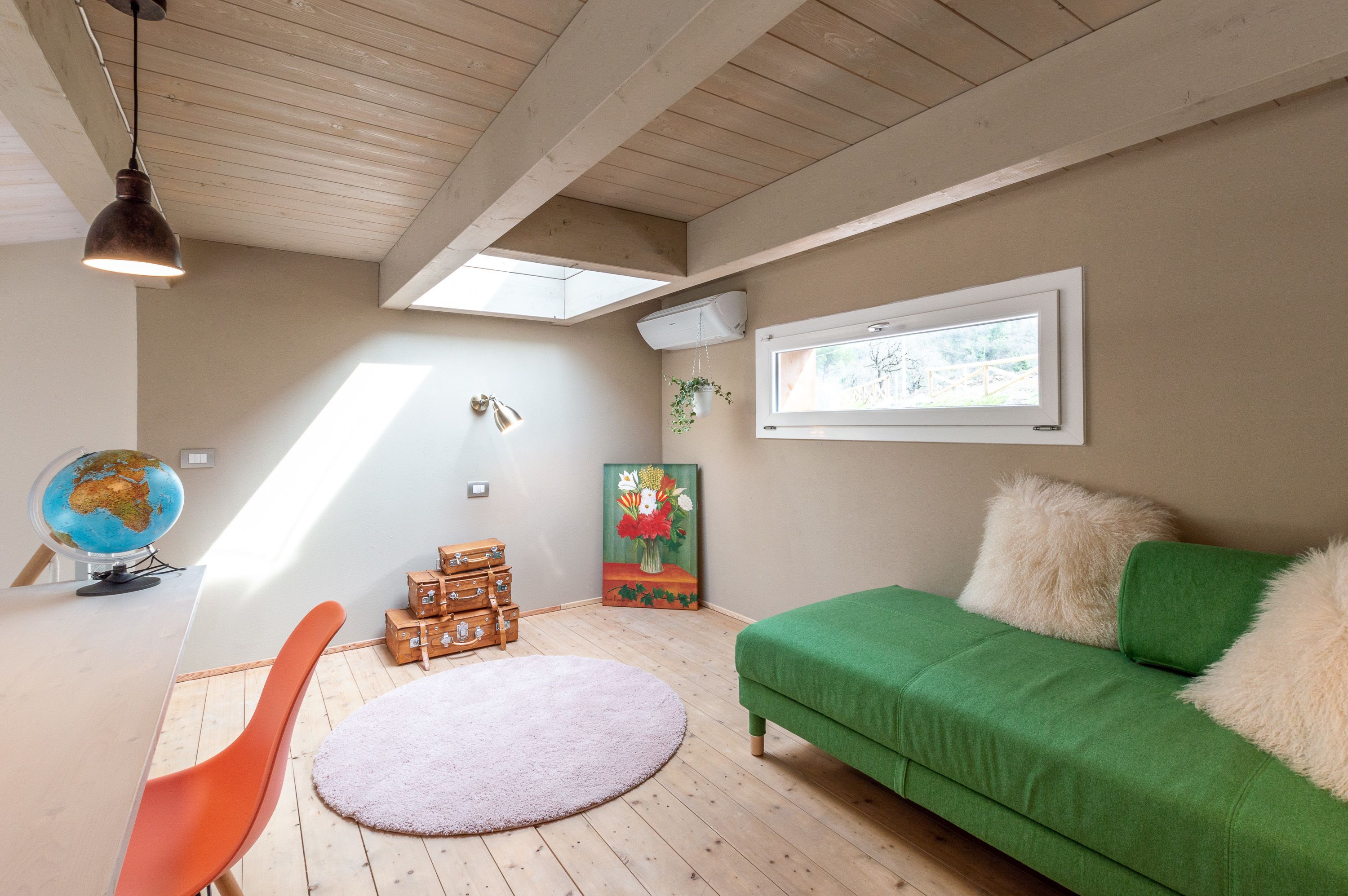 Um quarto com um sofá verde, um globo, uma pintura e piso de madeira.