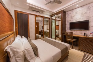 Quarto de hotel com cama, escrivaninha, cadeira, televisão e armário.