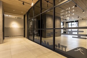 Um saguão de hotel moderno, com divisórias de vidro, placas de quarto numeradas e o perfil de um horizonte urbano no chão.