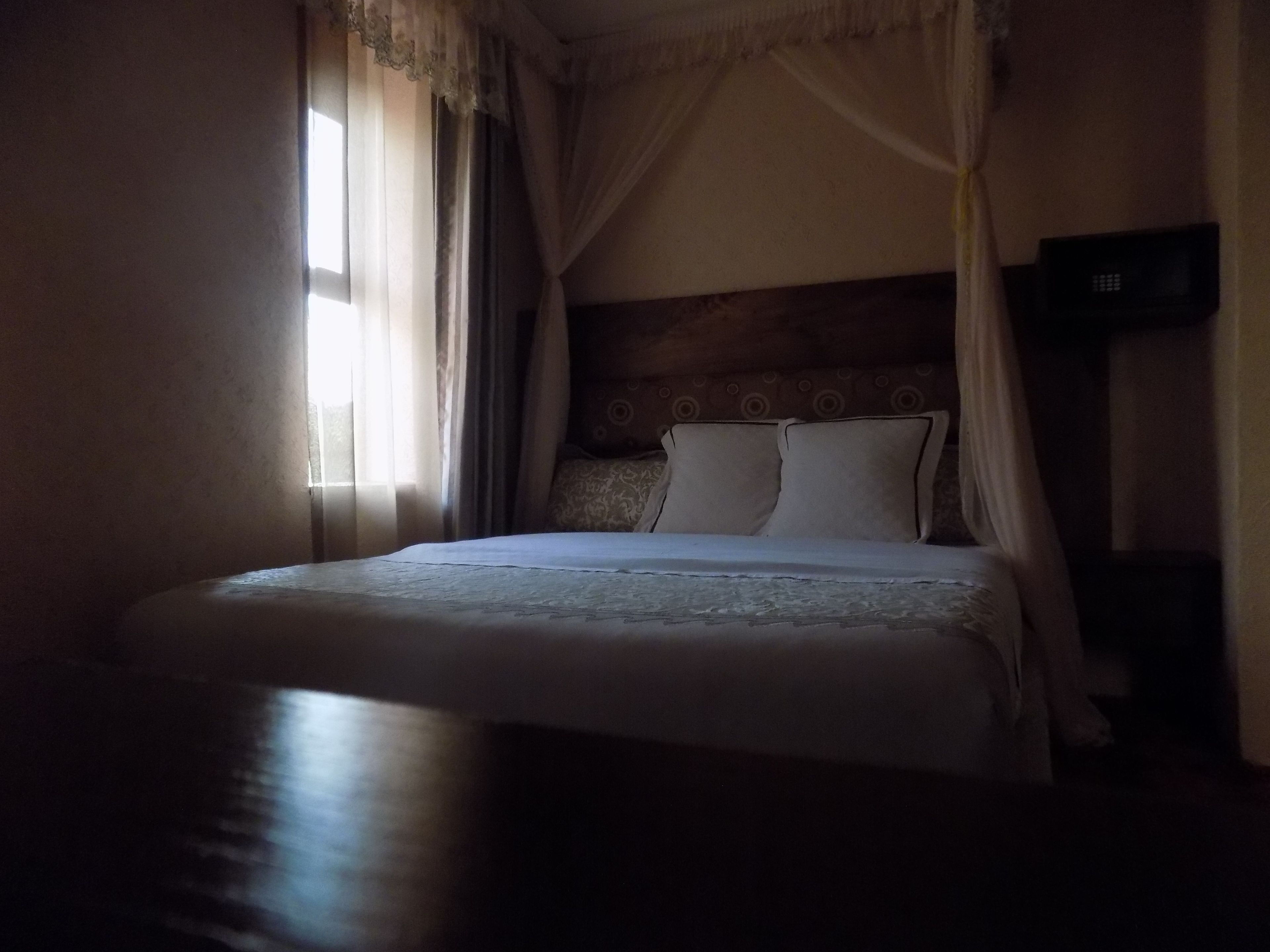 Um quarto com iluminação suave, uma cama, cortinas e uma cabeceira de madeira.