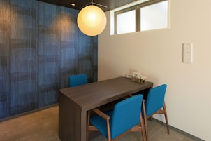 Uma sala de jantar moderna com uma mesa de madeira escura, cadeiras azuis, um lustre e uma janela com persianas.