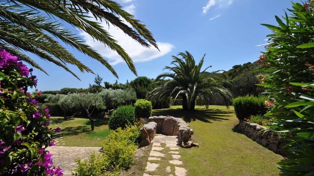 Um jardim com um caminho de pedra que leva a uma área de estar rodeada por vegetação exuberante e plantas floridas.