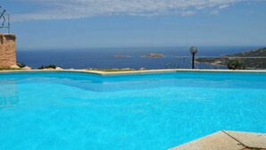 Uma piscina azul cristalina com vista para o mar e ilhas ao longe.