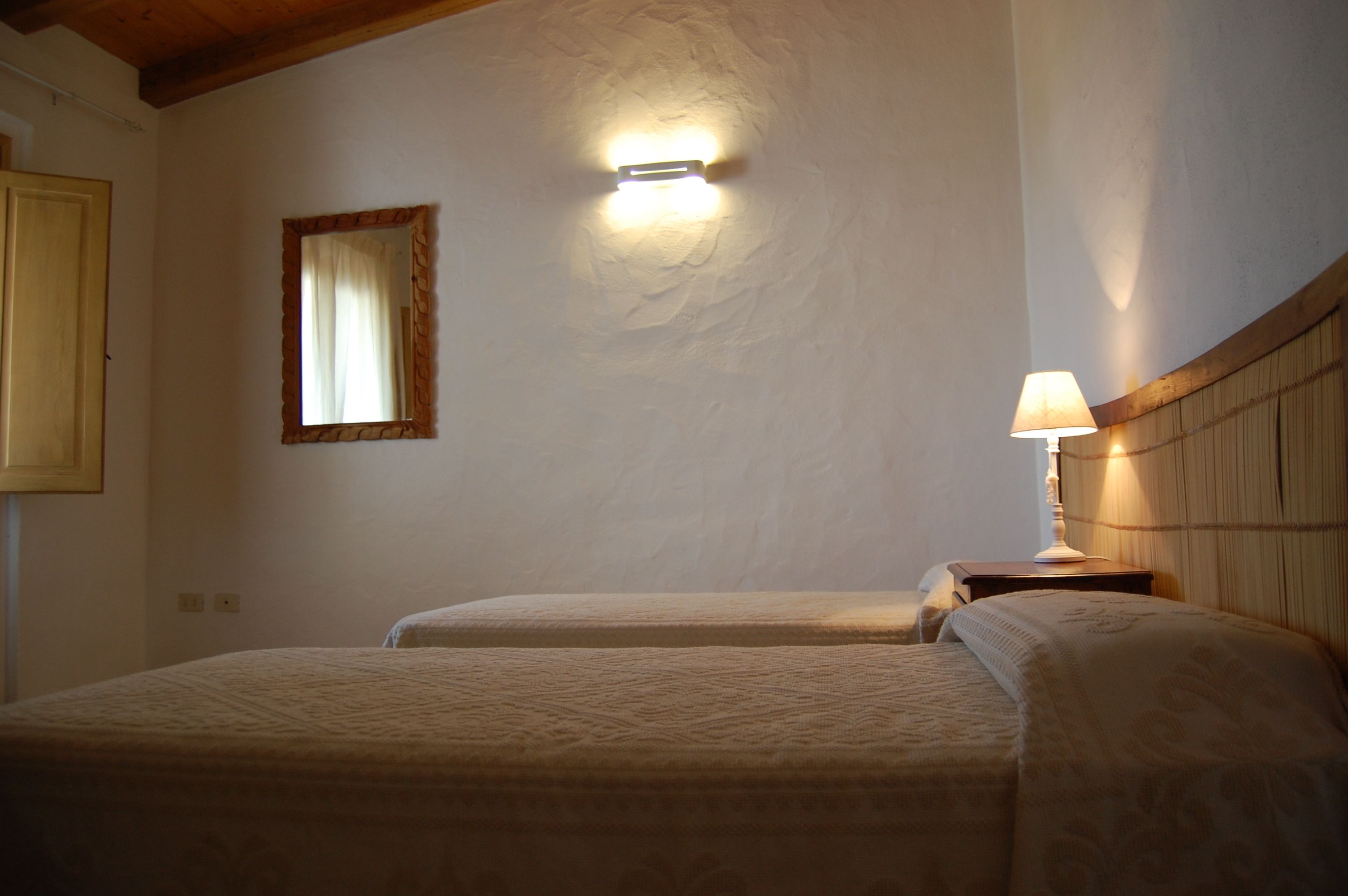 Quarto com duas camas, mesa de cabeceira com abajur, espelho e luminária na parede.