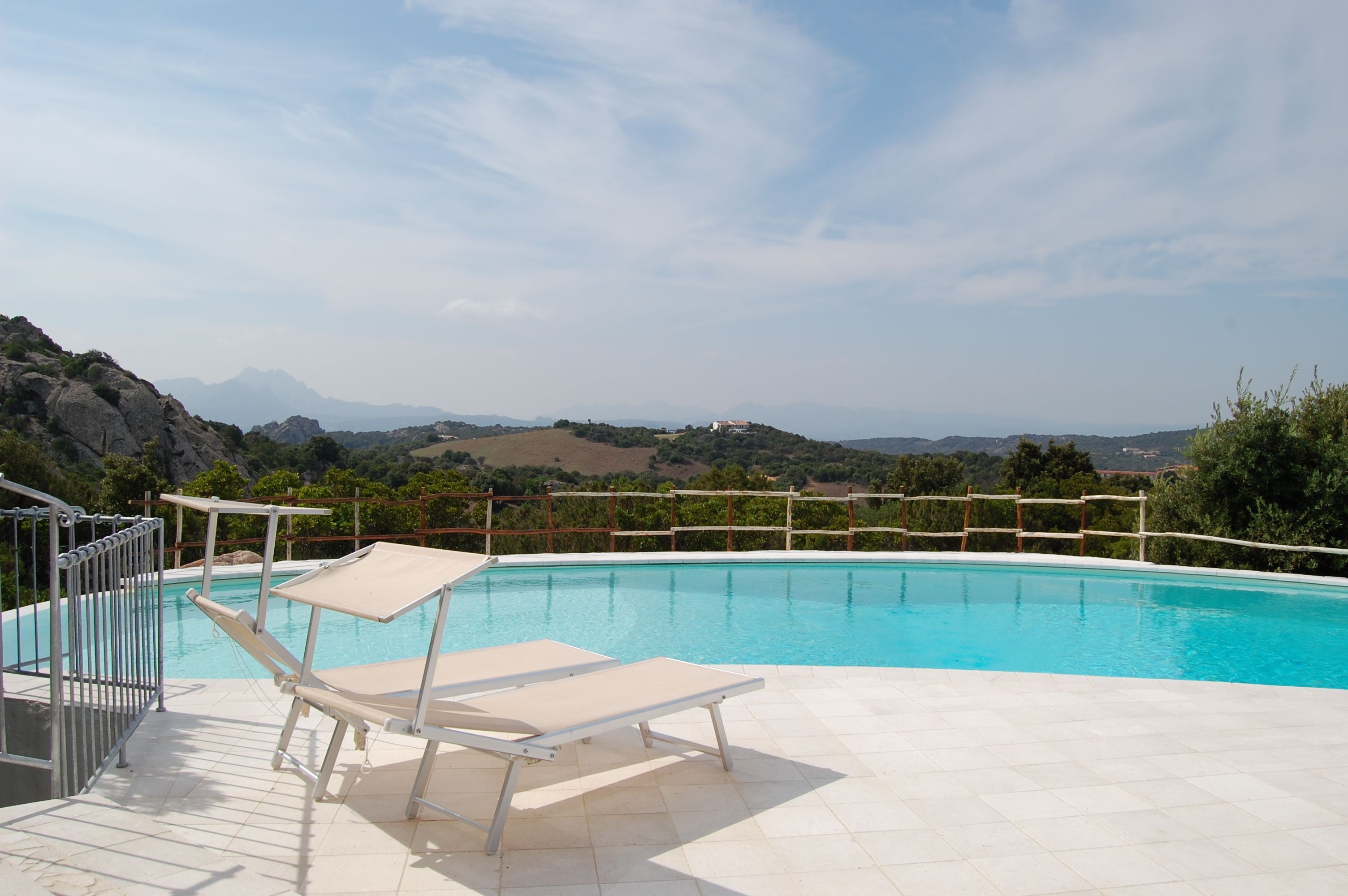 Piscina com espreguiçadeiras, um deck revestido e vista para colinas e montanhas ao longe.