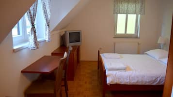 Quarto com cama, escrivaninha, televisão e janela com cortinas.