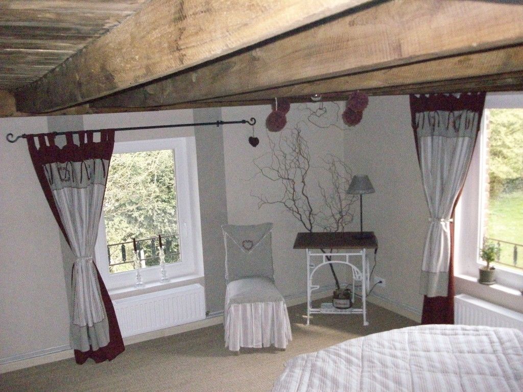 Quarto com cama, uma cadeira, uma mesinha de cabeceira com abajur e vista para o verde lá fora.