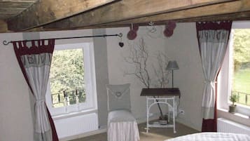 Quarto com cama, uma cadeira, uma mesinha de cabeceira com abajur e vista para o verde lá fora.