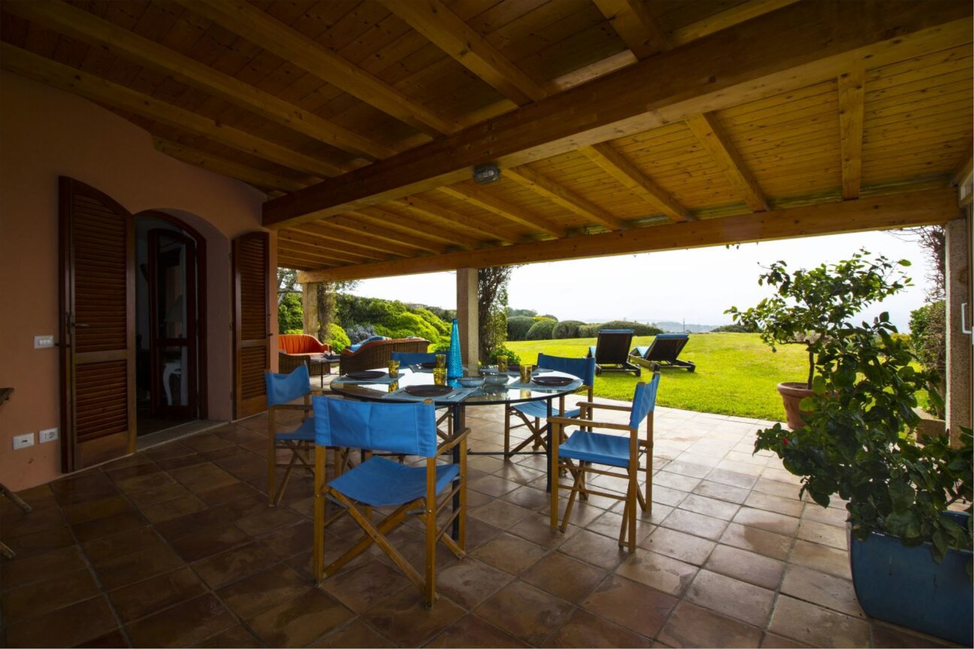 Um pátio externo com teto de madeira, uma mesa posta para refeições e cadeiras.