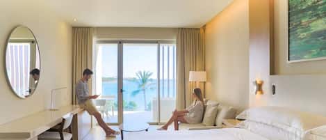 Quarto de hotel com cama, escrivaninha, cadeira, janela ampla com vista e um quadro na parede.