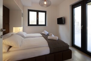 Quarto moderno com uma cama grande, TV fixada na parede e janela com vista externa.