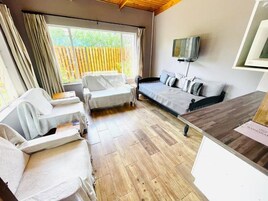 Quarto com cama, duas cadeiras, televisão e janela com cortinas.