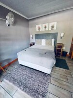 Quarto com cama grande, ventoinha no teto e cabeceira com luminárias fixadas na parede.